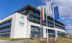 Edifício moderno do Tisia Hotel & Spa com várias varandas, amplas janelas de vidro e bandeiras, incluindo as bandeiras italiana, da União Europeia e do Tisia.
