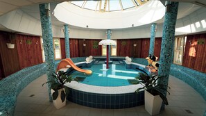 Uma grande piscina coberta com um escorregador, rodeada por paredes de madeira e pisos azulejados em azul.