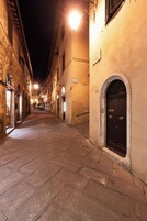 Uma rua estreita com calçada de pedra, edifícios históricos e letreiros iluminados.