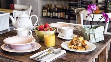 Uma mesa de café da manhã com uma chaleira, xícaras, uma tigela de morangos, um copo de suco de laranja e um prato de comida.