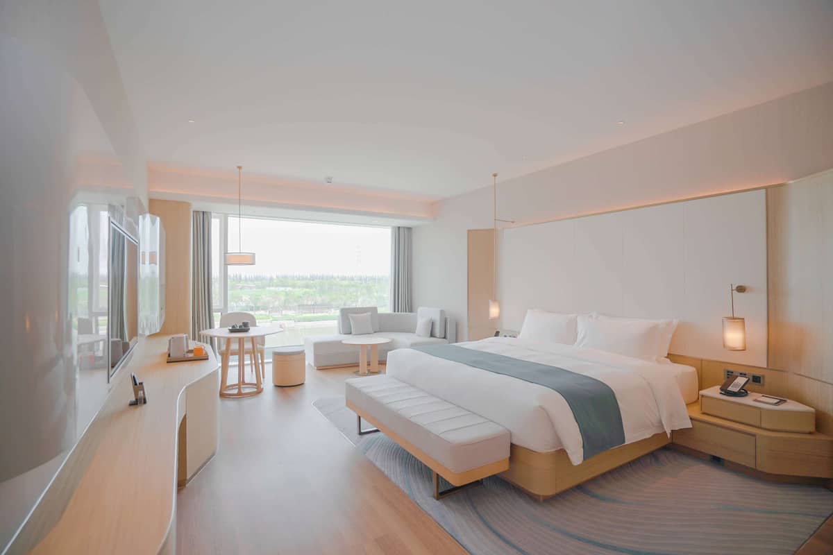 Quarto de hotel moderno com uma cama grande, um sofá, uma mesa de trabalho e vista para o exterior.