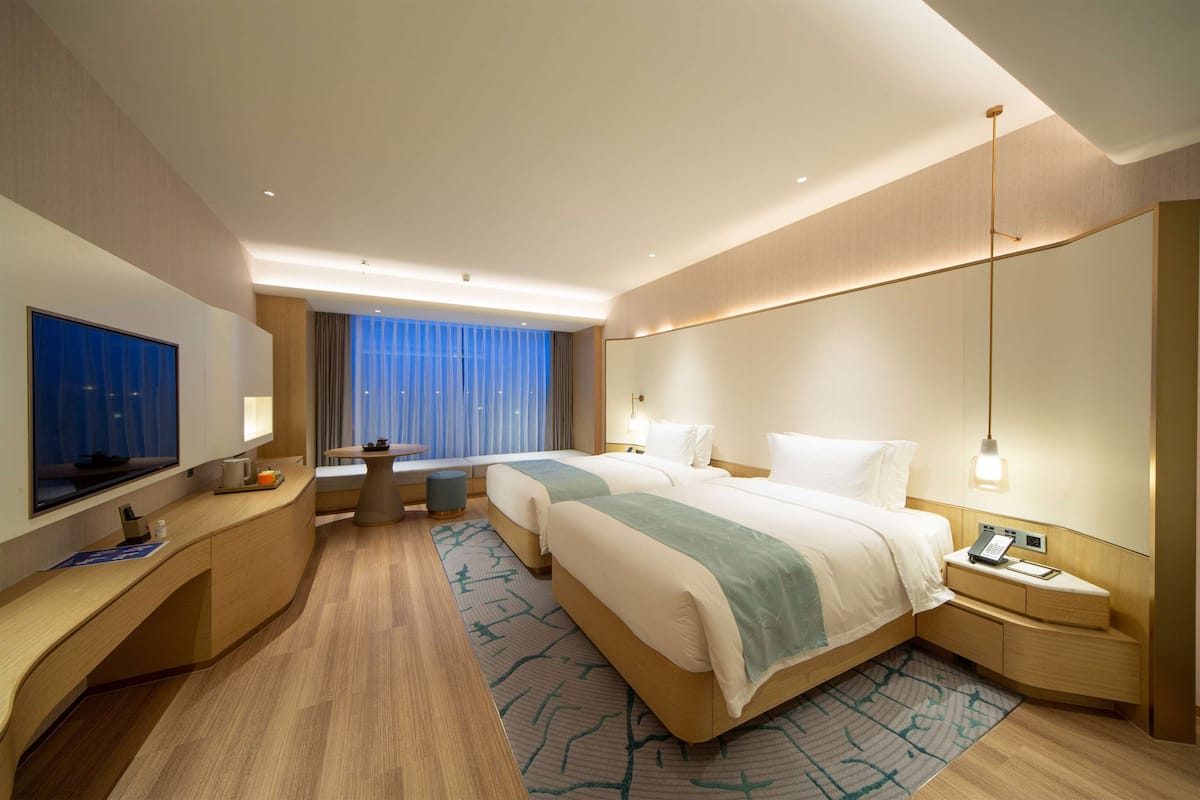 Quarto de hotel moderno com uma cama grande, mesas de cabeceira, uma escrivaninha e uma televisão.