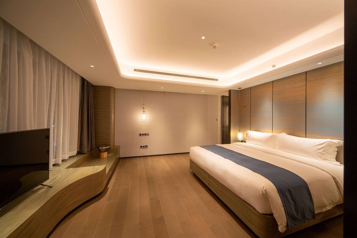 Quarto de hotel moderno com uma cama grande, uma TV de tela plana e um aparador de madeira.
