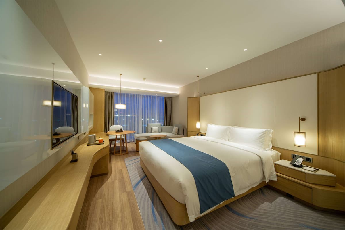 Quarto de hotel moderno com uma cama grande, mesas de cabeceira, uma escrivaninha e um espaço de estar.