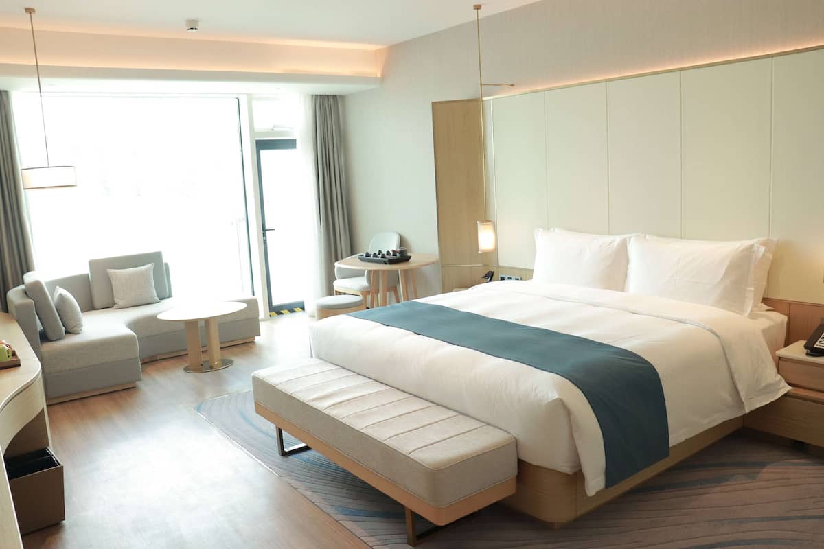 Quarto de hotel moderno com uma cama grande, um sofá, uma pequena mesa e um banco.