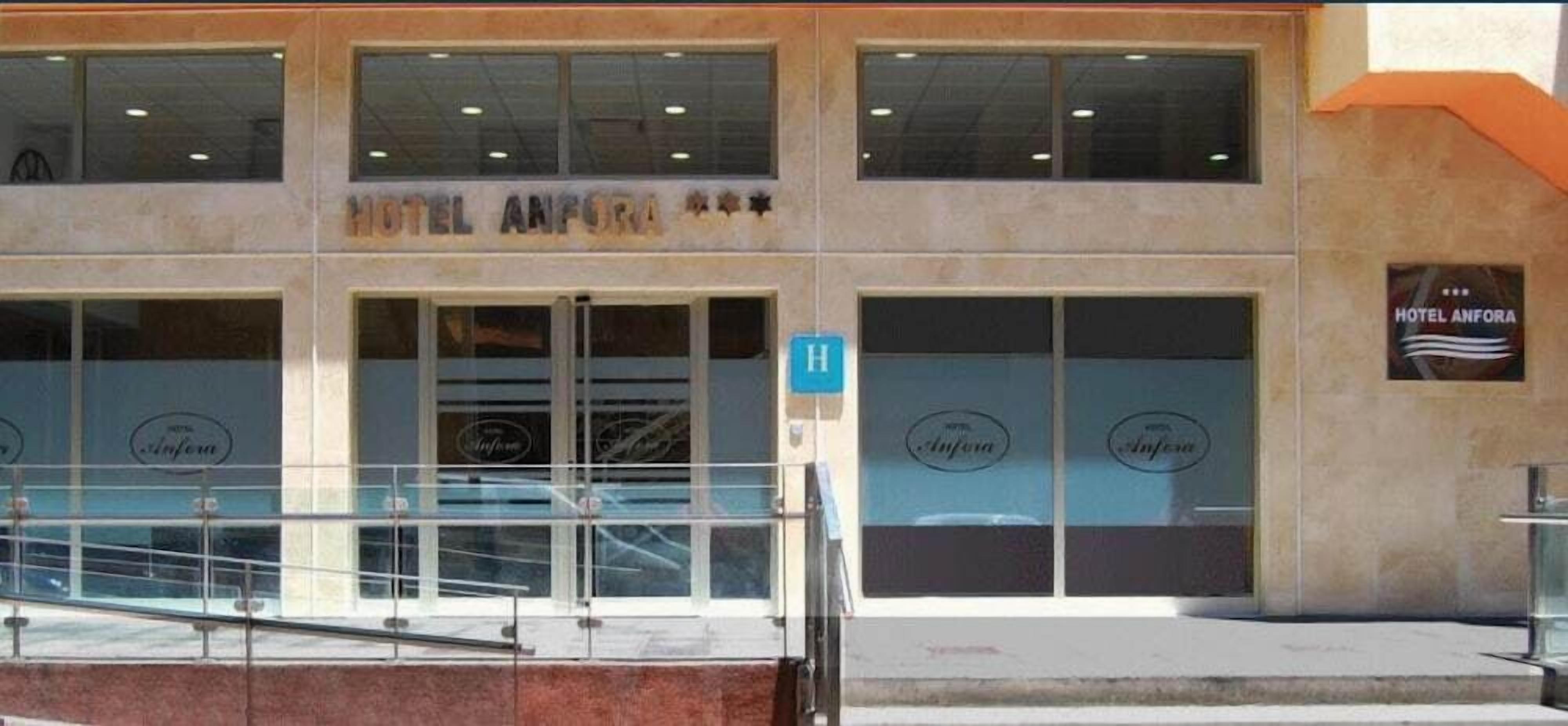 Fachada de hotel com grandes janelas, uma placa azul indicando hospedagem e uma escadaria que leva à entrada.