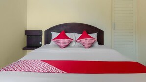 Cama bem arrumada com colcha branca e vermelha, dois travesseiros vermelhos com desenhos brancos e cabeceira de madeira escura.