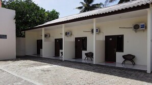 Um edifício com um caminho de azulejos que leva a uma área coberta com várias portas e aparelhos de ar condicionado.