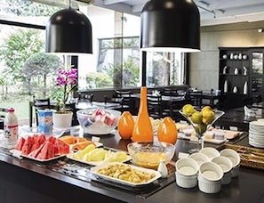 Buffet com diversos alimentos e bebidas, incluindo melancia, maçãs e suco de laranja.