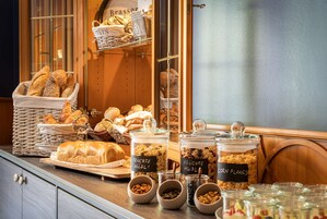 Buffet de café da manhã com pães, bolos e opções de cereais.
