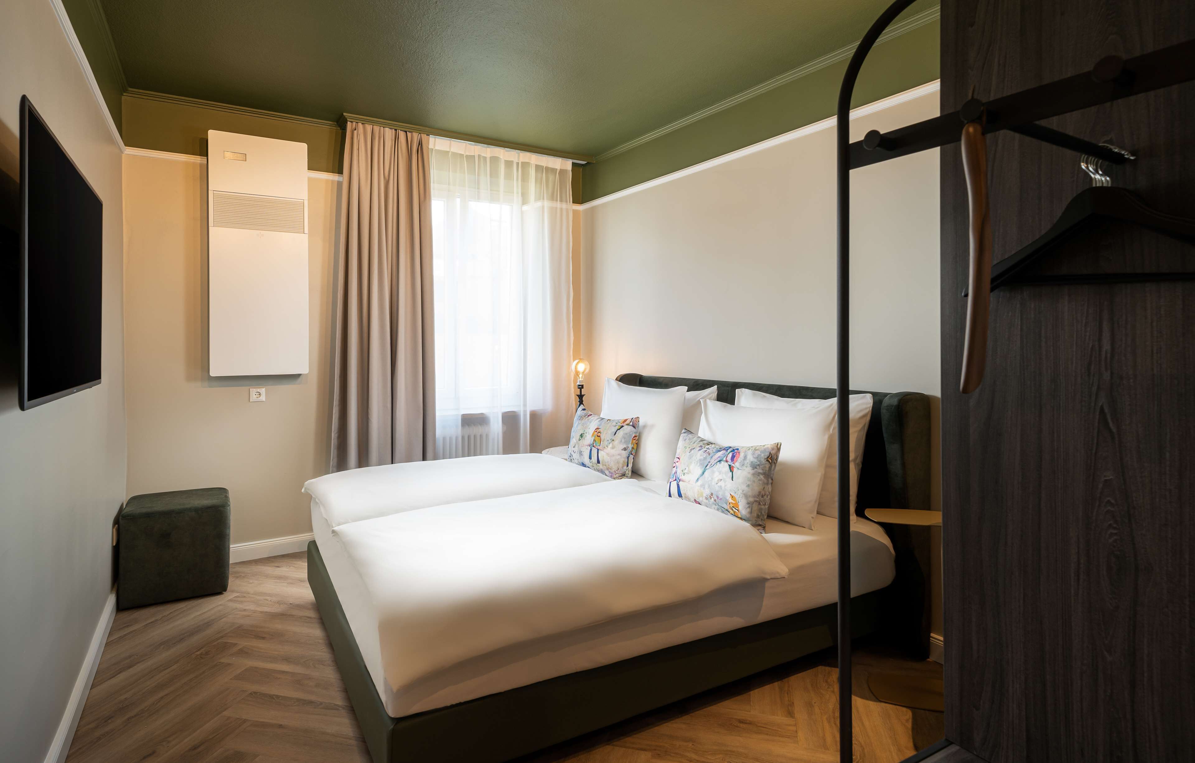 Quarto de hotel com uma cama grande, televisão de tela plana na parede, janela com cortinas e piso de madeira.