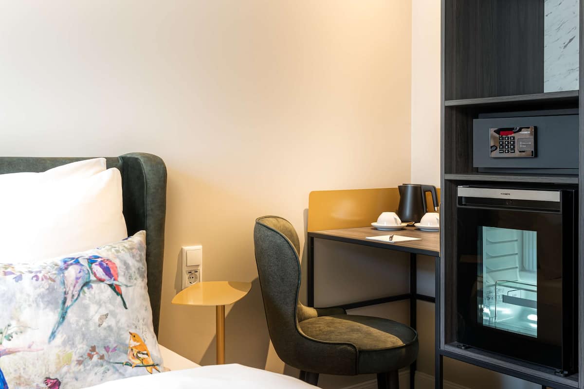 Quarto de hotel com cama, escrivaninha, cadeira, minibar e forno embutido.