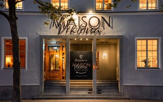Entrada de hotel com uma placa que diz "MAISON Viktoria EINGANG | ENTRANCE" e um endereço de site.