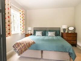 Quarto com cama, duas mesas de cabeceira, cômoda, janela com cortinas e abajur.