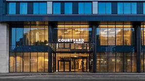 Entrada de hotel moderna com grandes janelas de vidro e uma placa com a inscrição 'COURTYARD BY MARRIOTT'.