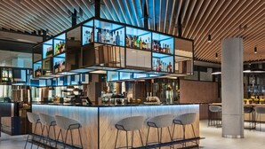 Uma área de bar moderna com um balcão central, diversas prateleiras cheias de garrafas e banquetas.