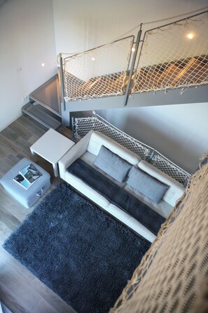 Um quarto moderno no estilo loft, com um sofá branco, uma mesinha pequena branca, um tapete azul escuro e uma rede.