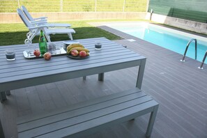 Mesa à beira da piscina com uma garrafa, copos e frutas.