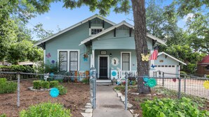 Uma casa azul clara com varanda frontal, caixa de correio e um pequeno jardim com flores decorativas.