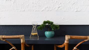 Uma área de refeições com mesa preta, duas cadeiras de bambu, um vaso verde-água com uma planta e uma ampulheta.