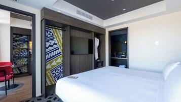 Quarto de hotel com uma cama grande, televisão, guarda-roupa e uma cadeira vermelha.
