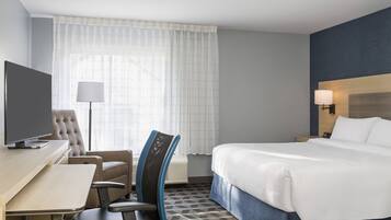 Quarto de hotel com cama, escrivaninha com computador, cadeira, abajur e televisão.