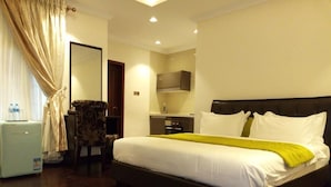 Quarto de hotel com uma cama grande, uma escrivaninha, uma cadeira, um espelho e uma cozinha compacta.