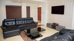 Uma sala de estar moderna com um sofá de couro preto, uma mesa de centro de vidro e uma TV de tela plana na parede.
