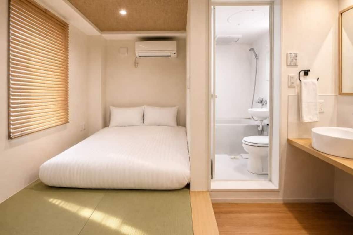 Quarto pequeno com cama, vaso sanitário e pia.