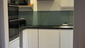 Uma cozinha compacta com armários brancos, bancada preta, micro-ondas e torradeira.