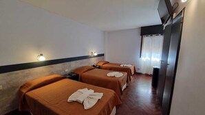 Quarto de hotel com quatro camas, cada uma com um edredom castanho e uma toalha. Há luminárias fixadas na parede e uma TV de tela plana na parede.