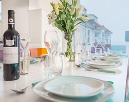 Mesa posta para refeição, com uma garrafa de vinho, um vaso de flores e vista para um edifício.