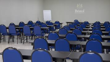Uma sala de conferências com fileiras de cadeiras azuis e mesas, uma lousa branca e um projetor no teto.