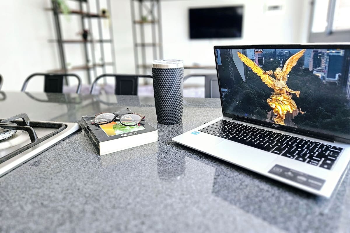 Um laptop exibindo uma estátua dourada, um copo e um par de óculos sobre uma mesa.