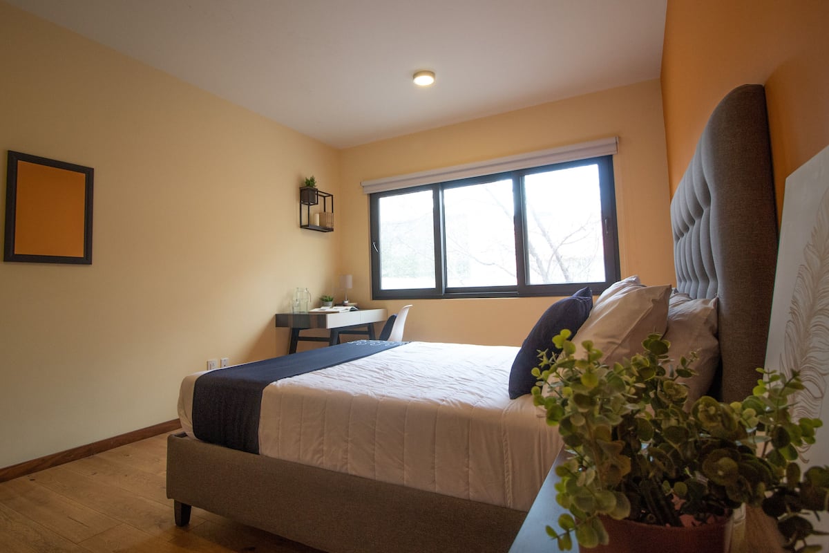 Um quarto com uma cama, uma escrivaninha e uma janela.
