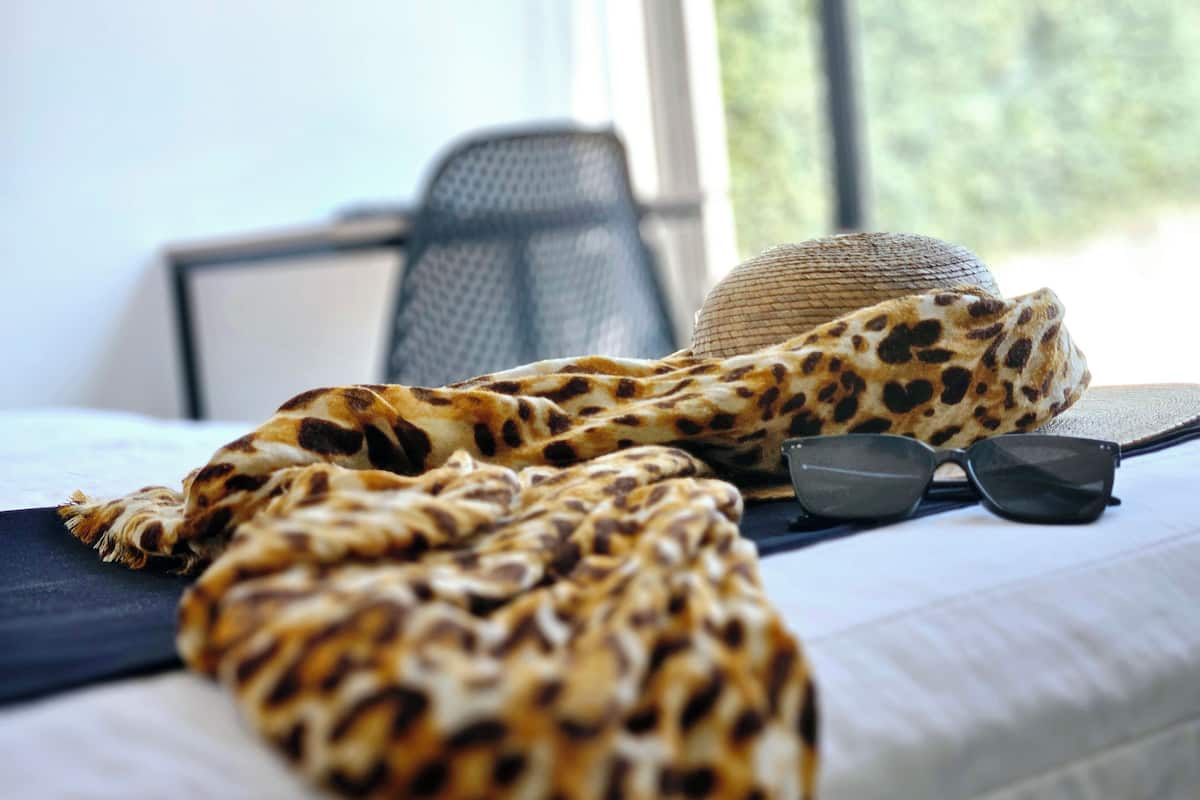 Uma cama com um cobertor estampado com onças, um chapéu de palha e óculos de sol.