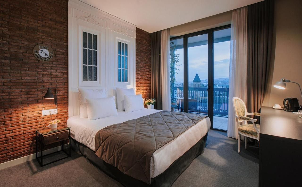 Quarto de hotel com uma cama grande, uma escrivaninha, uma cadeira, uma janela com vista e uma parede de tijolos.