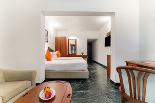 Quarto de hotel com uma cama, uma escrivaninha de madeira, uma cadeira, um sofá e um prato de frutas na escrivaninha.