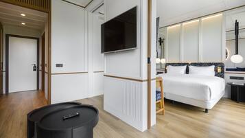 Quarto de hotel moderno com uma cama grande, televisão de tela plana na parede, uma mesinha e uma cadeira.