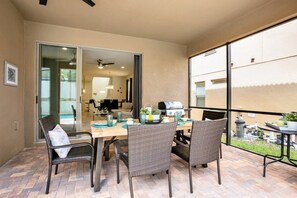 Um pátio externo com uma mesa de jantar, cadeiras de vime e uma churrasqueira.