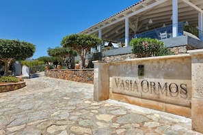 Uma trilha de pedra leva a um edifício com uma placa que diz 'Vasia Ormos'.