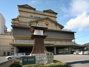 Um edifício com vários andares, uma torre central, um estacionamento e uma placa com caracteres japoneses.
