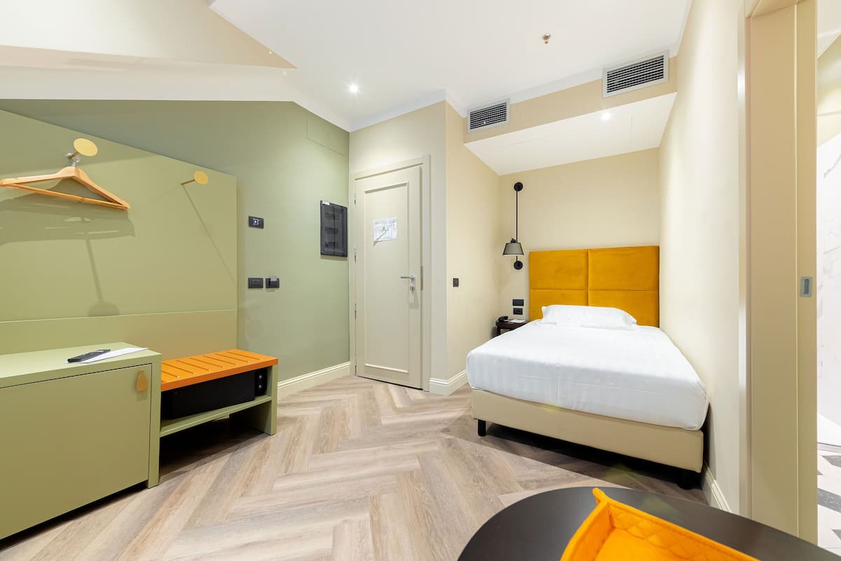 Quarto de hotel moderno com cama, escrivaninha, cadeira, guarda-roupa e espelho.