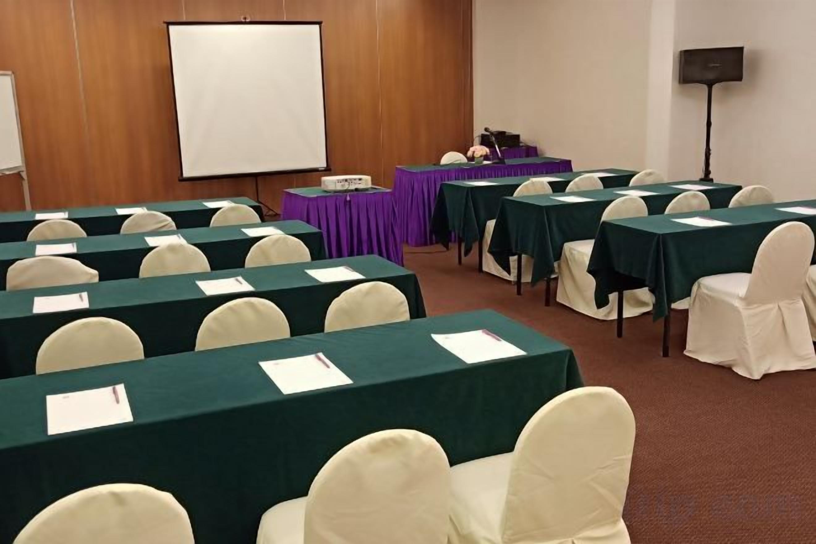 Uma sala de conferências com mesas, cadeiras dispostas em fileiras e uma tela de projeção.
