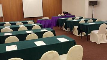 Uma sala de conferências com mesas, cadeiras dispostas em fileiras e uma tela de projeção.