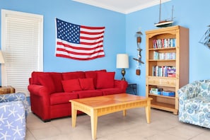 Uma sala de estar com um sofá vermelho, uma mesa de centro de madeira, uma estante e uma bandeira na parede.