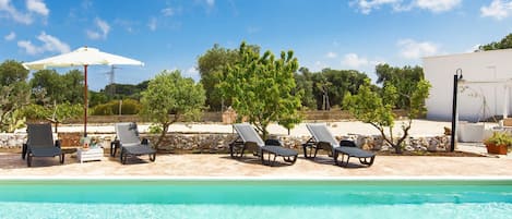 Área da piscina com espreguiçadeiras e um guarda-sol branco.