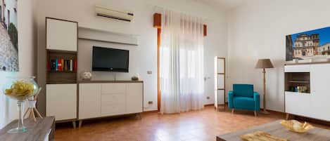 Uma sala de estar moderna com televisão de tela plana, armários brancos, uma poltrona azul e uma mesa de jantar com copos.