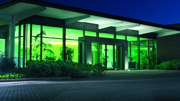 Um edifício moderno com grandes janelas de vidro e interior iluminado em tons de verde.