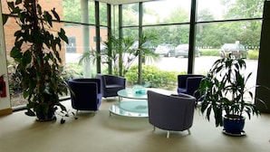 Um espaço interior moderno, com grandes janelas, diversas plantas em vasos e uma mesa de vidro central rodeada por cadeiras.